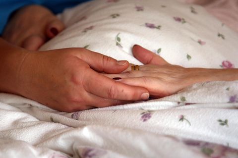 Die Hände einer Bewohnerin liegen in einem Hospiz auf einer Bettdecke