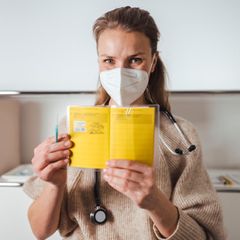 Corona: eine Ärztin mit Maske hält den gelben Impfpass in die Kamera