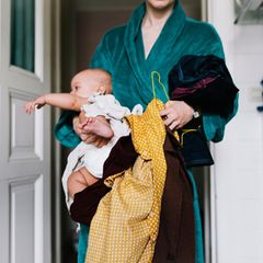 Alleinerziehende Mutter mit Kind und Kleidung auf dem Arm